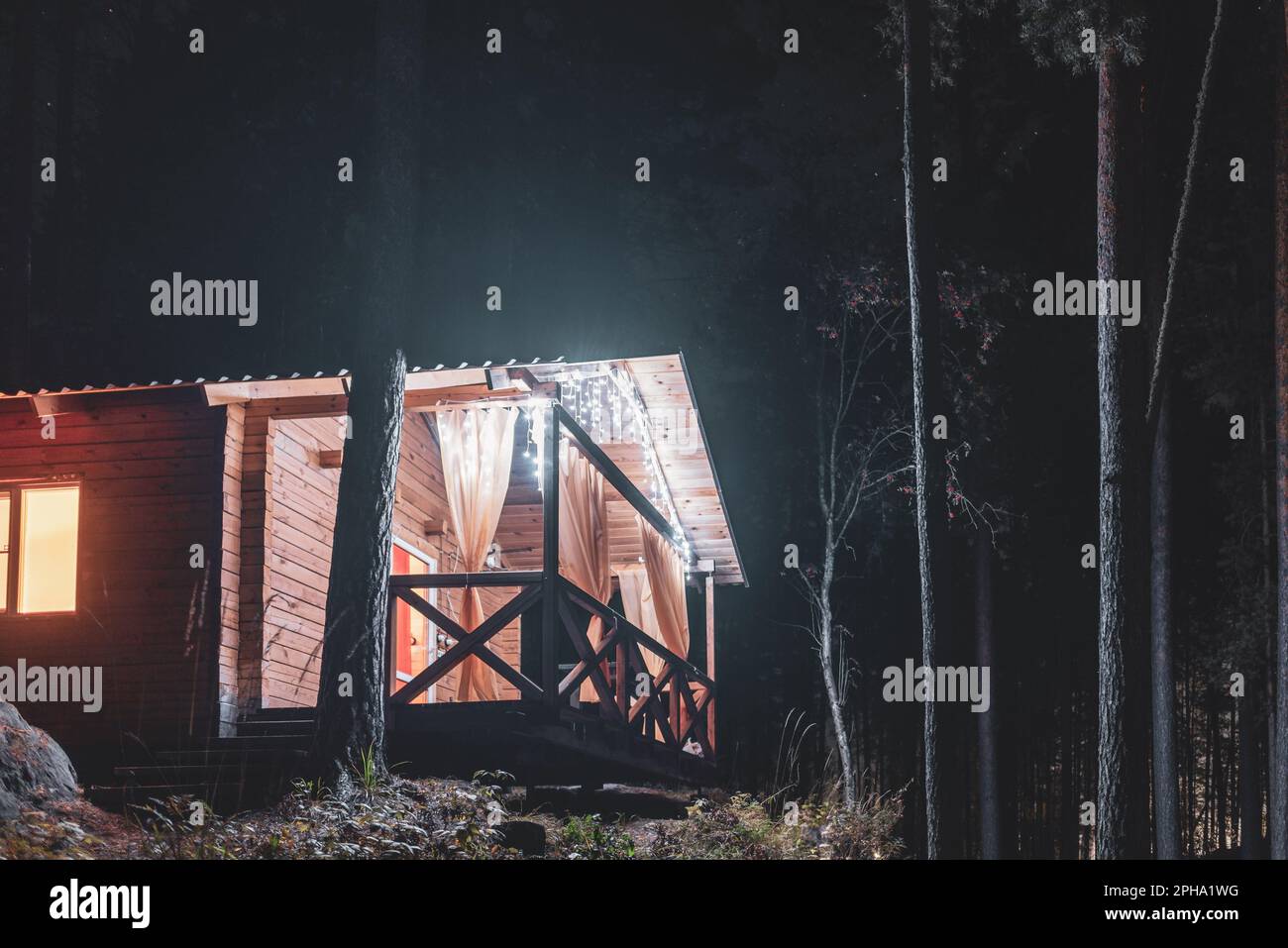 A wooden holiday cottage at night glows with garlands in the dark on a ...