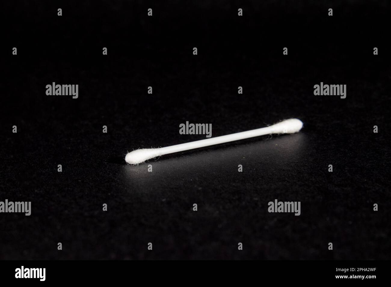 Picture of a single cotton swab, black, standing on black background ...