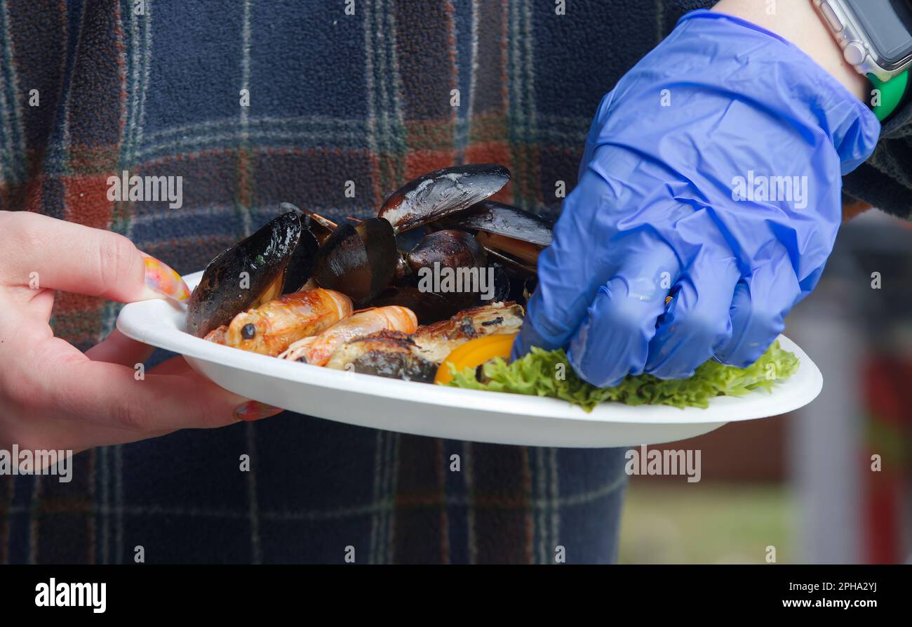 Eating sea food at a street food market, chef hands holding a plastic ...