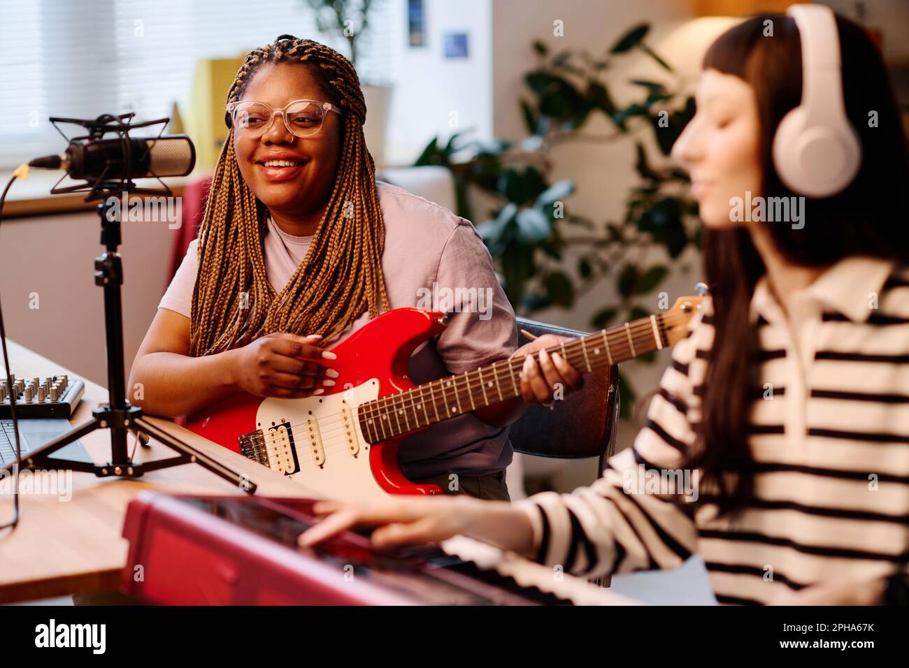 African American woman playing guitar and recording song together with ...