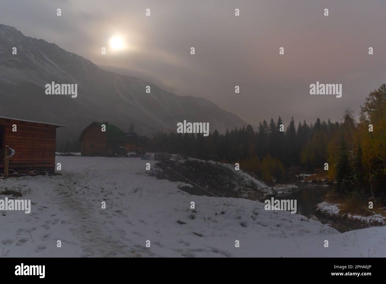 Cottages by the river near the forest on the snow under the mountain ...