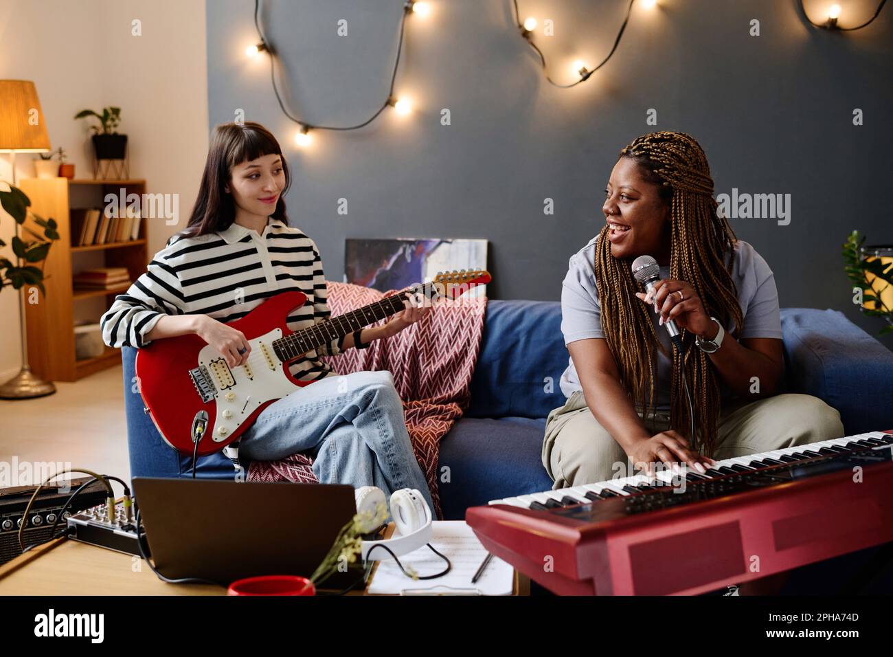 Two girls sitting on sofa and playing music together in studio using ...