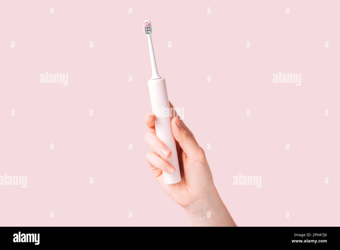 Electric toothbrush of pink color in female hand against pink ...