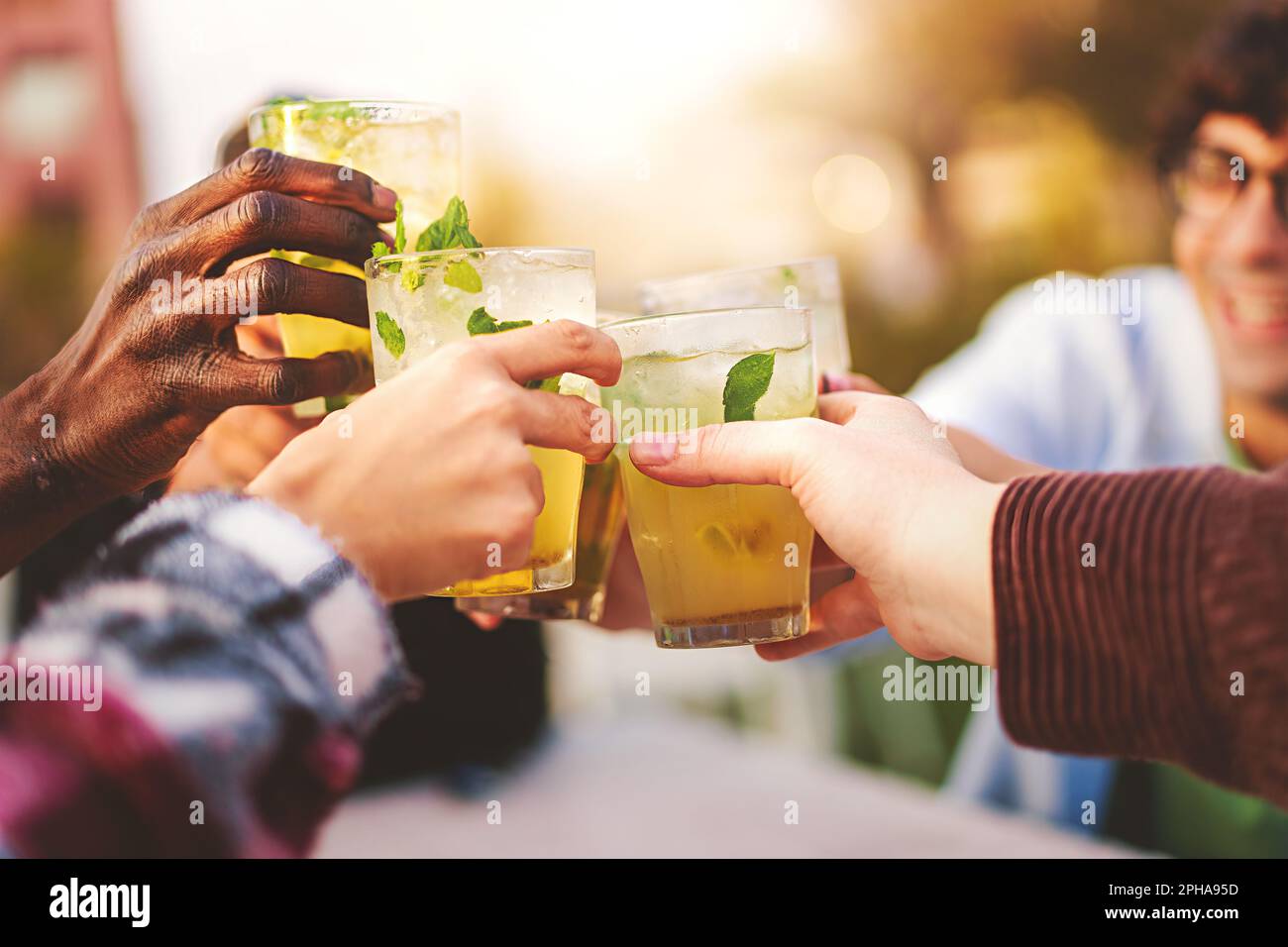 A group of multiracial friends gather at an outdoor bar and toast with ...