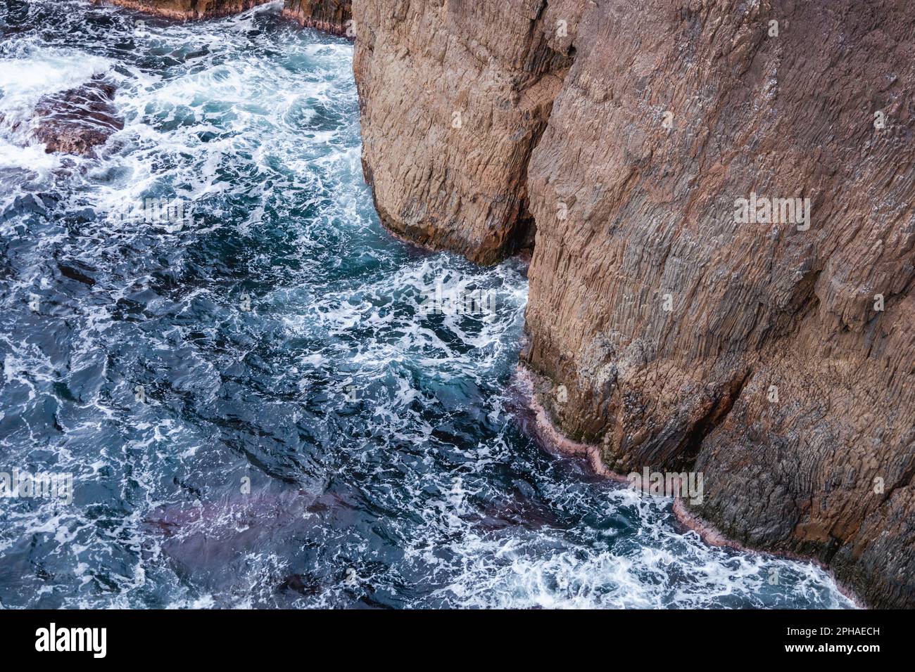 A rocky cliff, overlooking a vast expanse of vibrant blue ocean water ...
