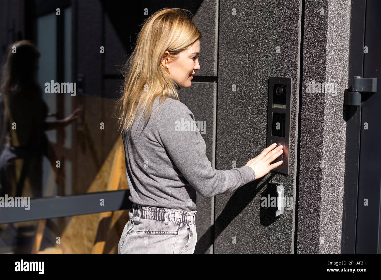 Happy woman ringing on doorbell at building entrance. Using intercom ...