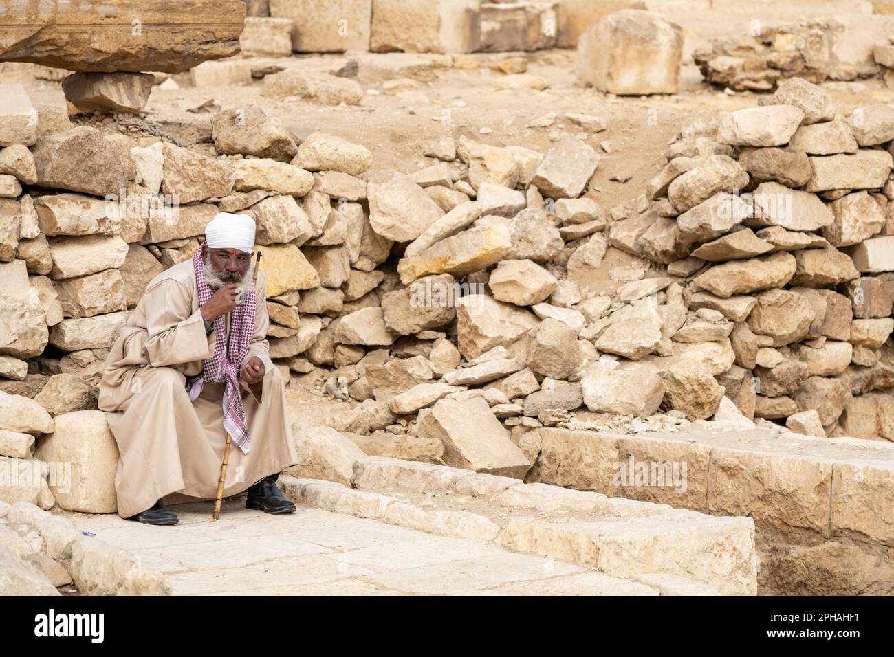 An old local man sitting on a rock at the Pyramids of Giza complex in ...