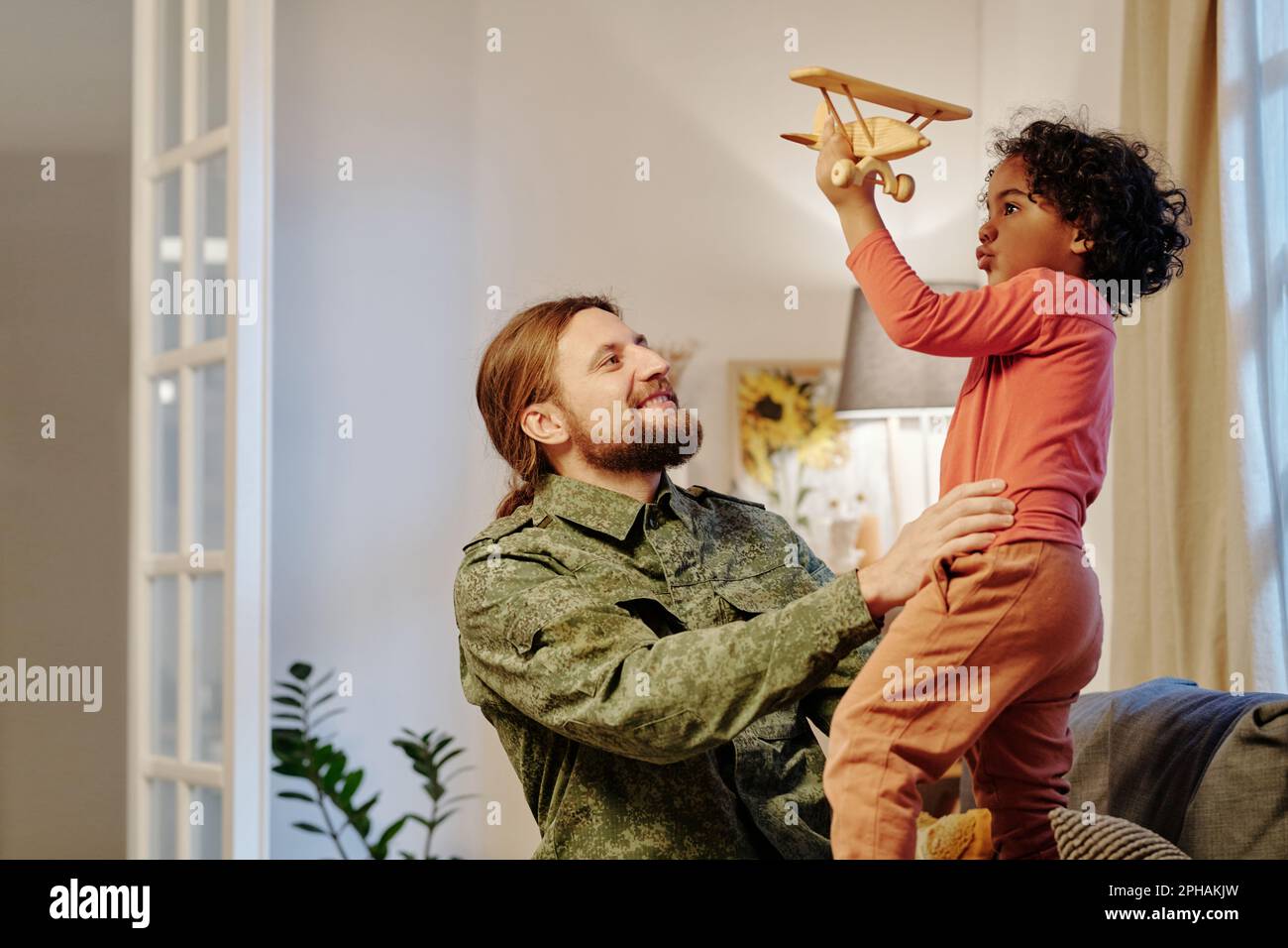 Happy young man in military uniform having fun with his cute little son ...