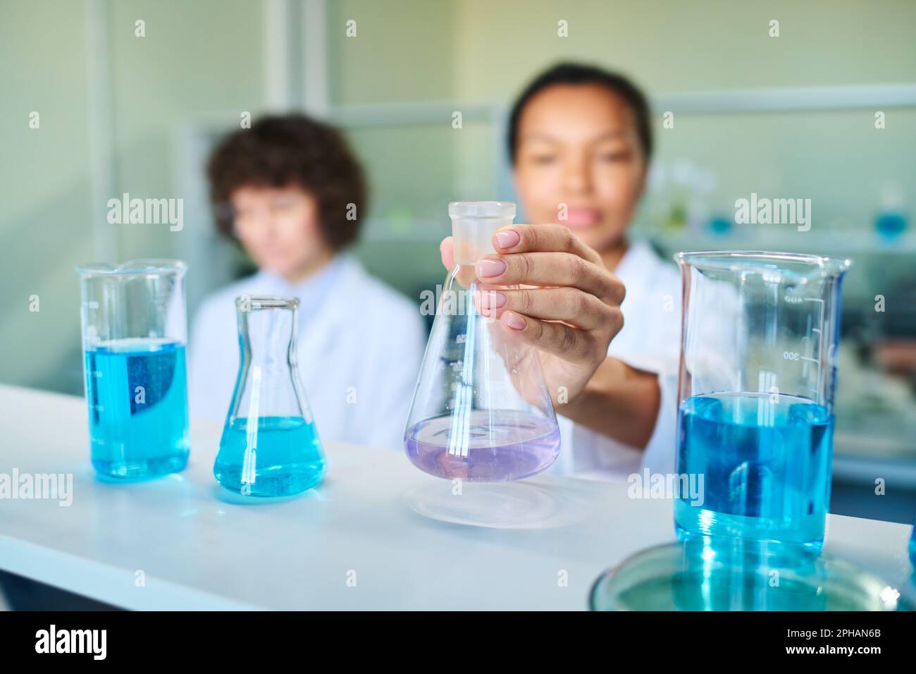 Selective focus on hand of young female clinician putting beaker with ...