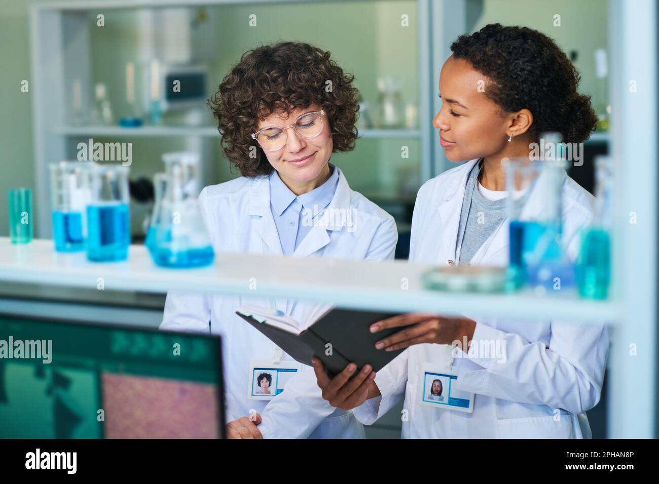 Young brunette female researcher in lab coat and eyeglasses looking at ...