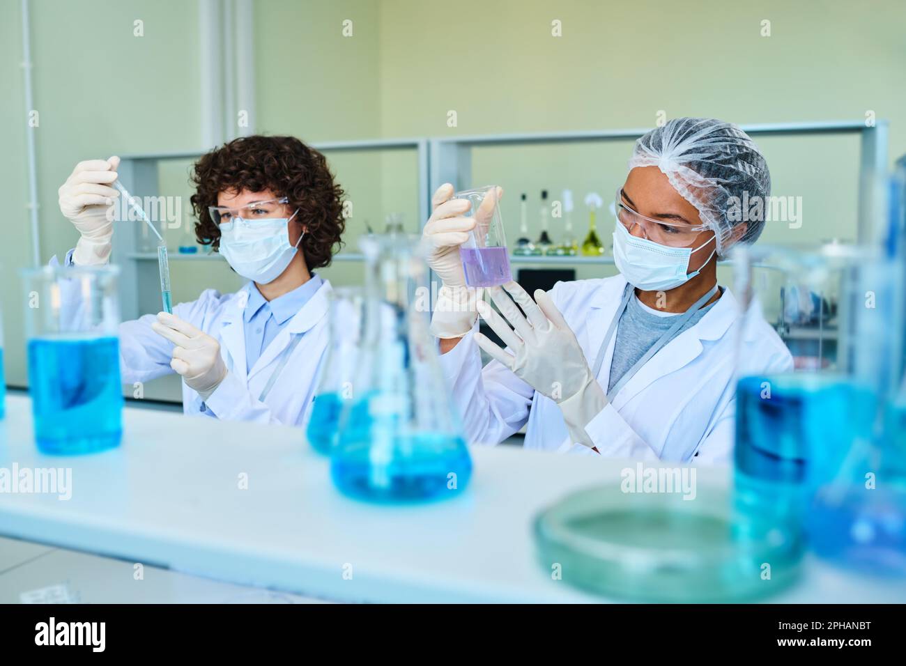 Two intercultural scientists in lab coats and protective masks studying ...