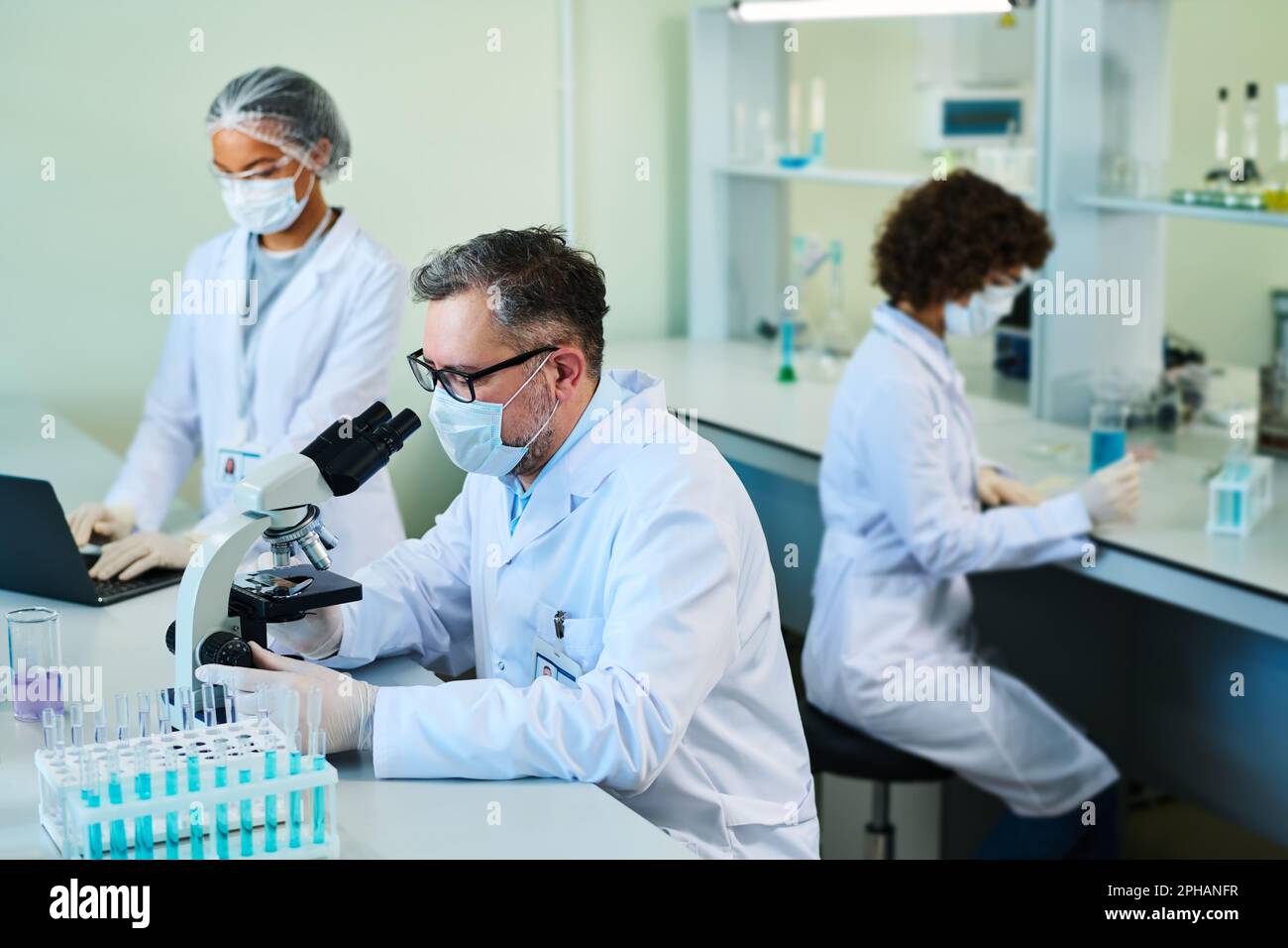Mature professional chemist or pharmacologist looking in microscope ...