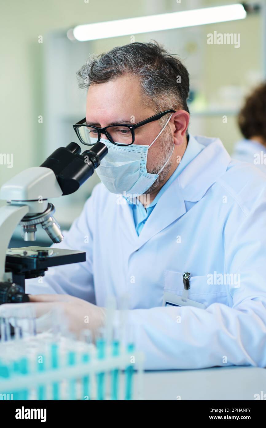 Mature expert in virology wearing lab coat, eyeglasses, protective mask ...