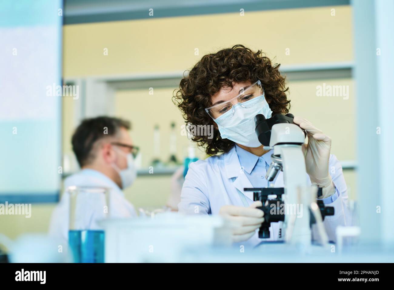 Mature expert in virology wearing protective mask adjusting dial on ...