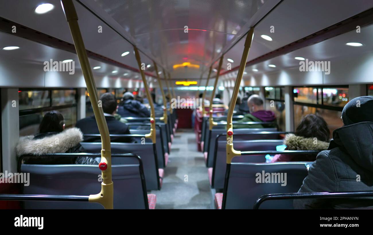 Back of bus with passengers at night in London traditional transportation. People commuting ...