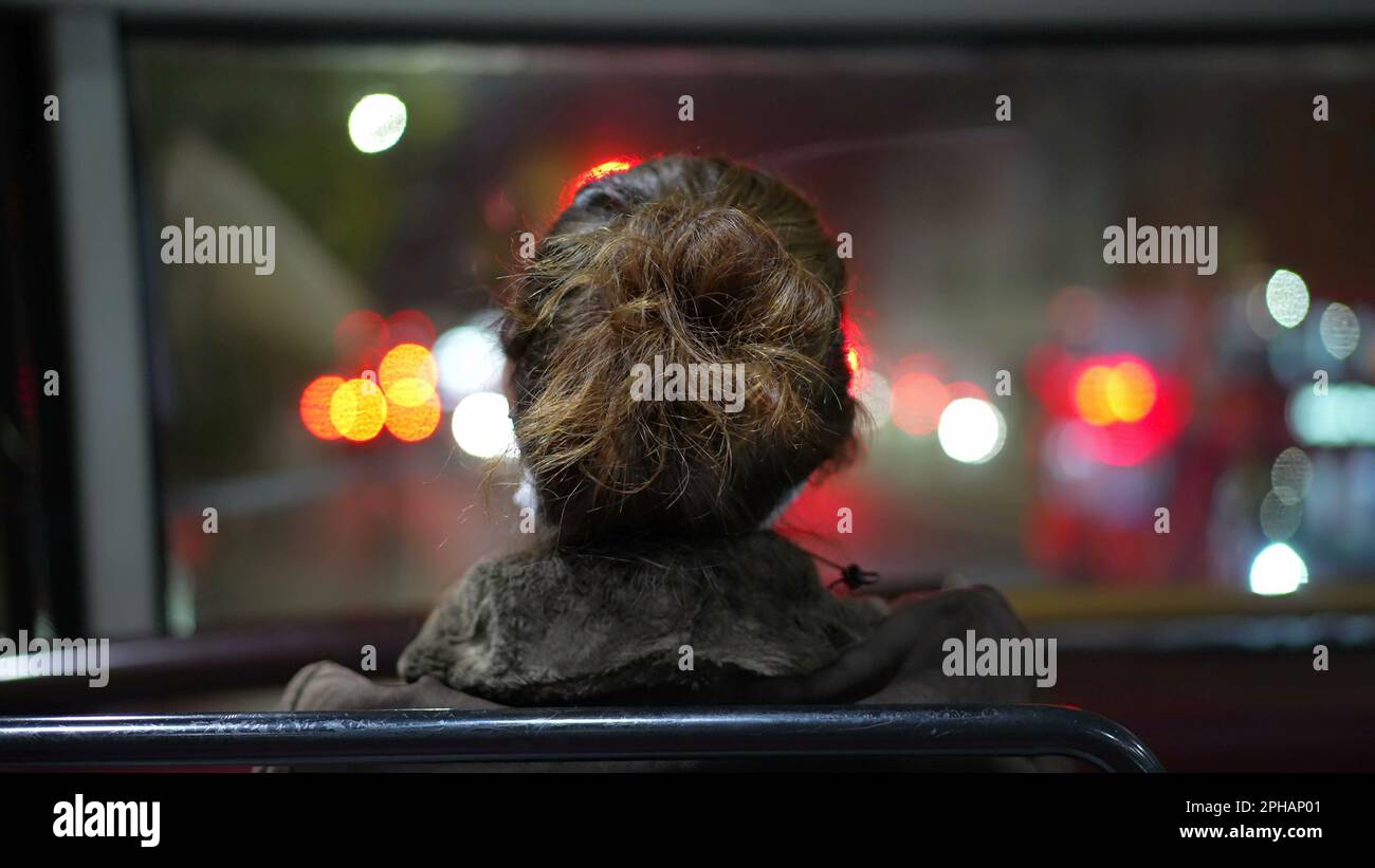 Back of female commuter riding bus at night after work. Passenger ...