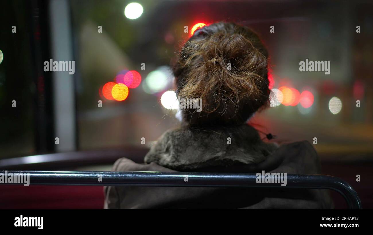 Back of female commuter riding bus at night after work. Passenger ...