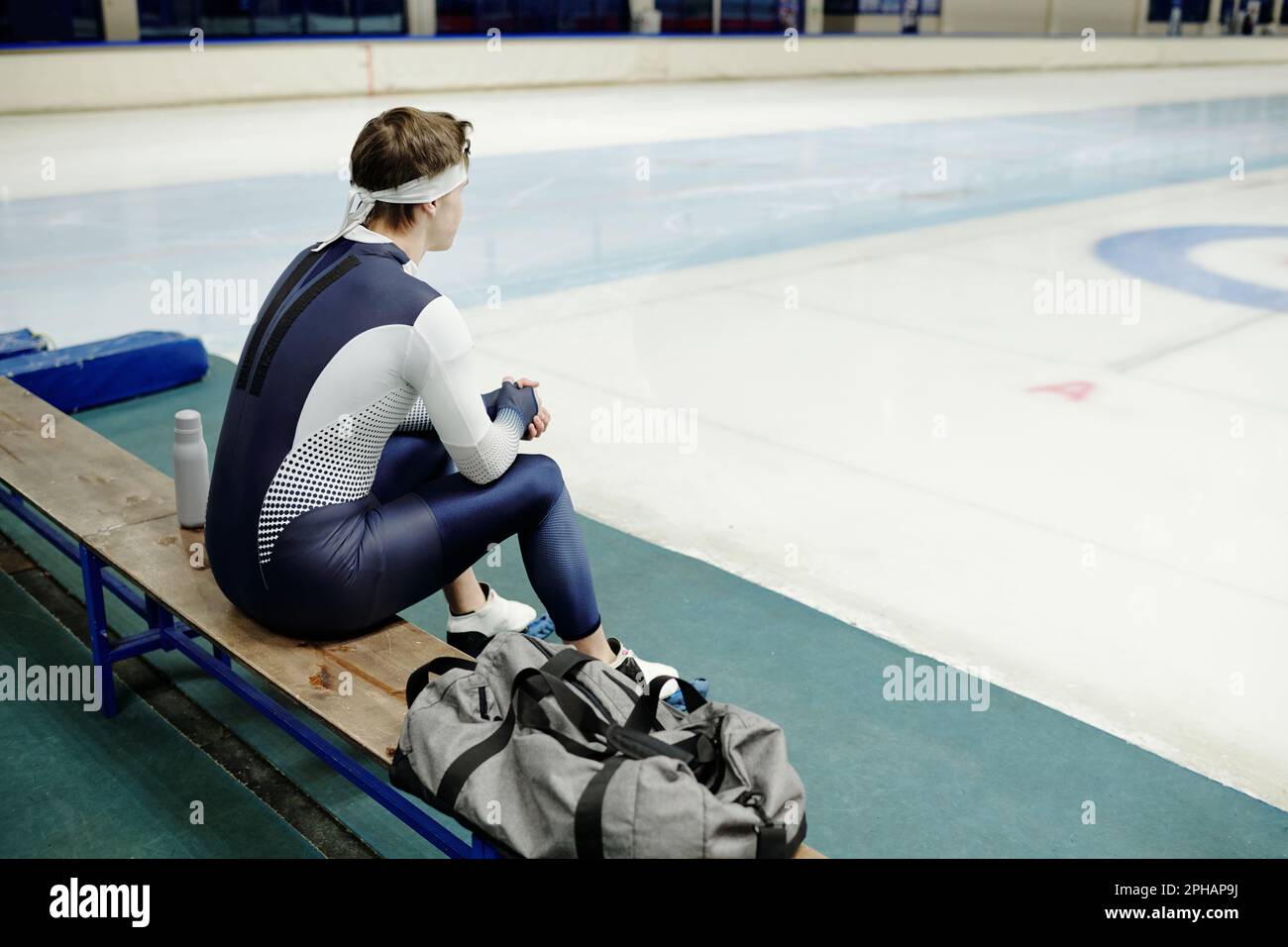 Rear view of young sportsman in speed skating uniform having rest while ...