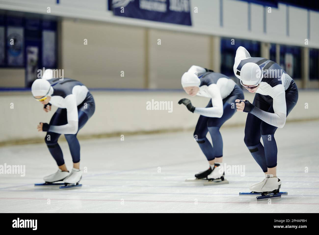 Group of fit youthful sportsmen in sports uniform sliding along ice ...