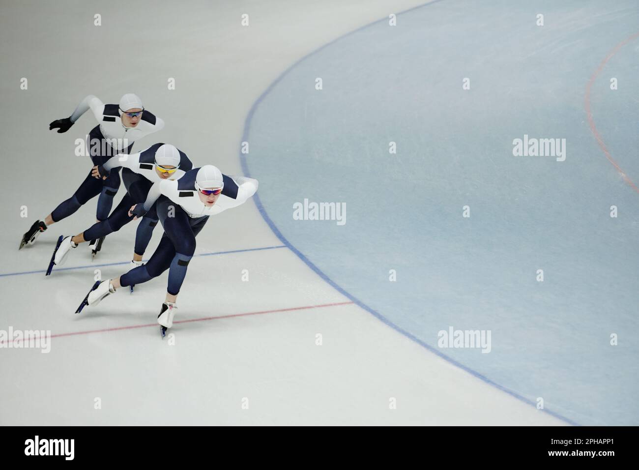 Row of three young active athletes on skates sliding along ice rink ...
