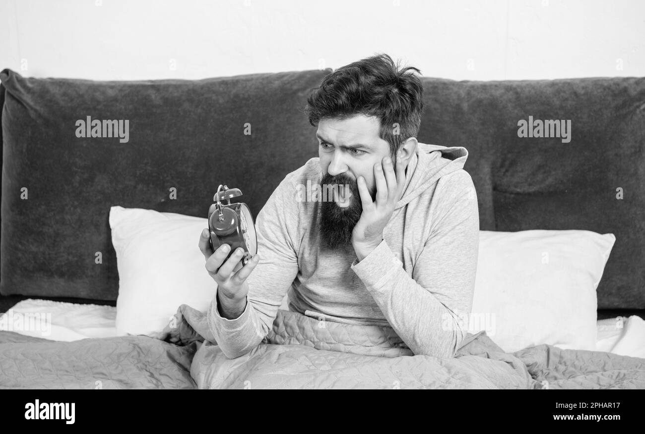 Awaken man shouting in panic looking at alarm clock in bed in morning ...
