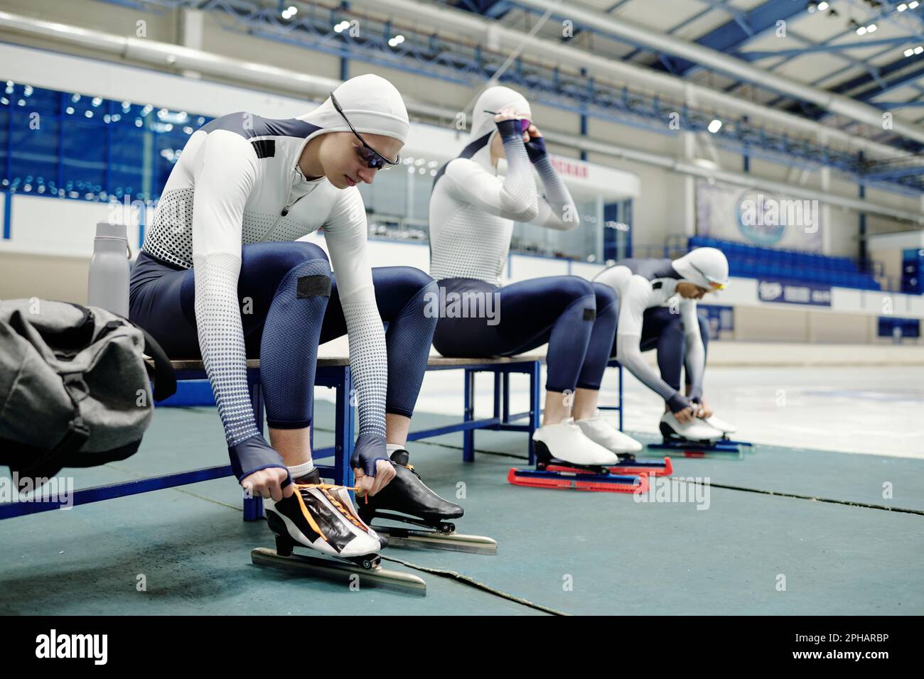 Group of restful speed skaters tying shoelaces on skates at break while ...