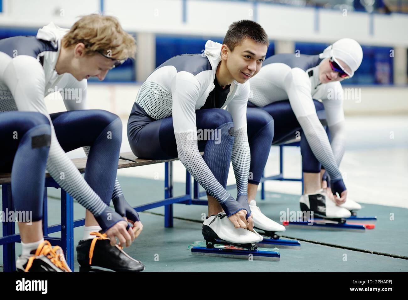 Three active guys in sports uniform tying shoelaces on skates at break ...