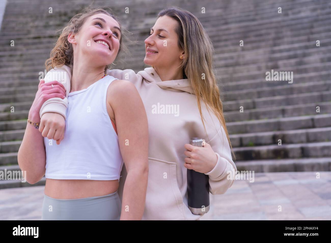 Two young female friends standing side by side and smiling happily ...