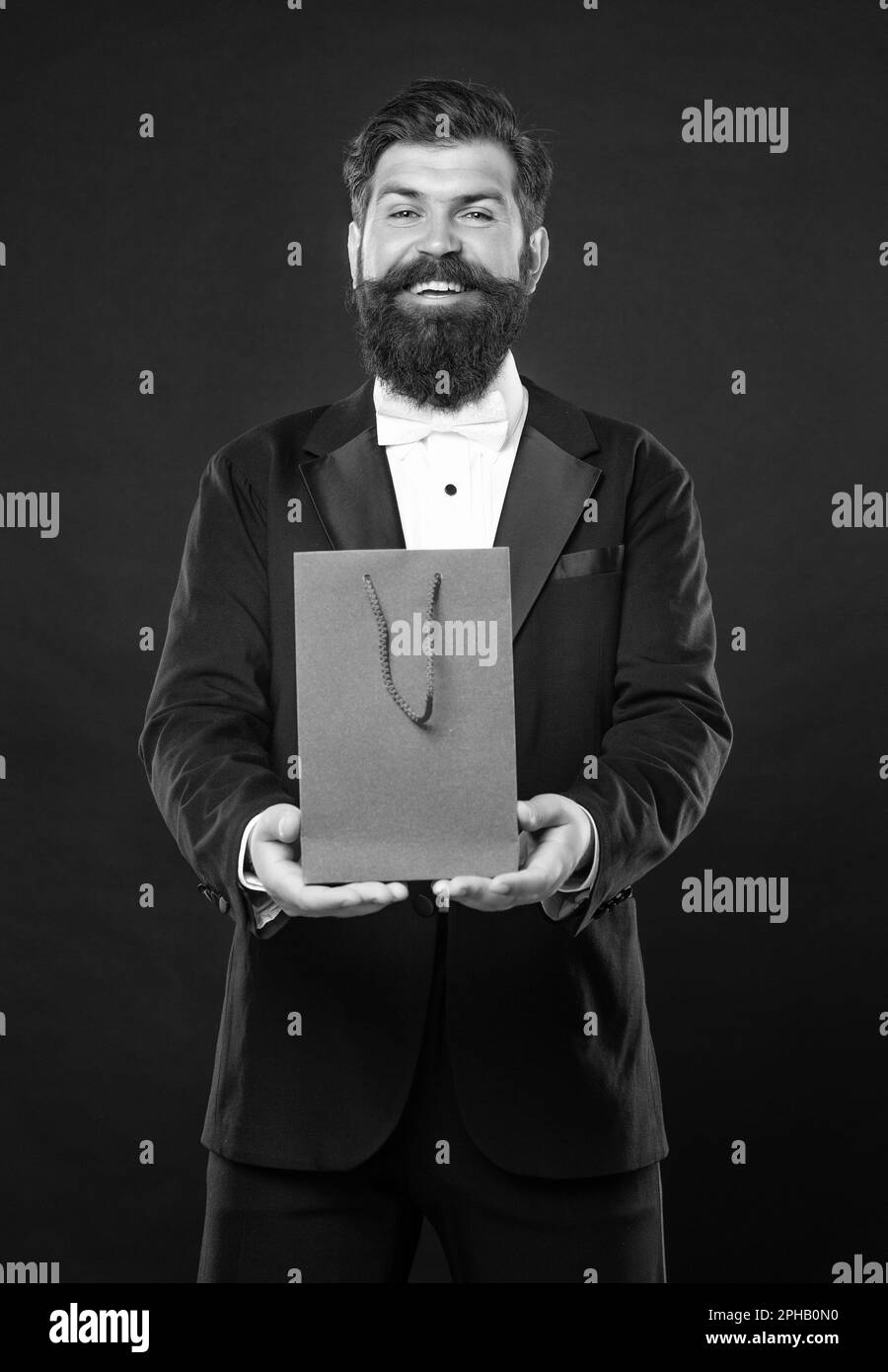 glad man in tuxedo bow tie on black background presenting purchase ...