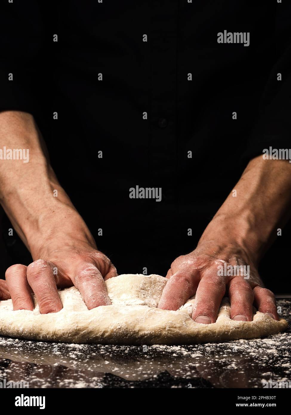 Baker or cook kneads an organic yeast dough, black background with ...