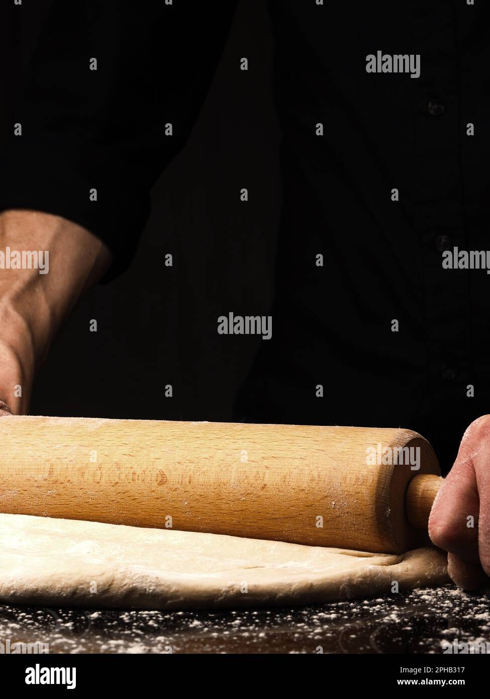 Baker or cook rolls out an organic yeast dough on the work surface ...