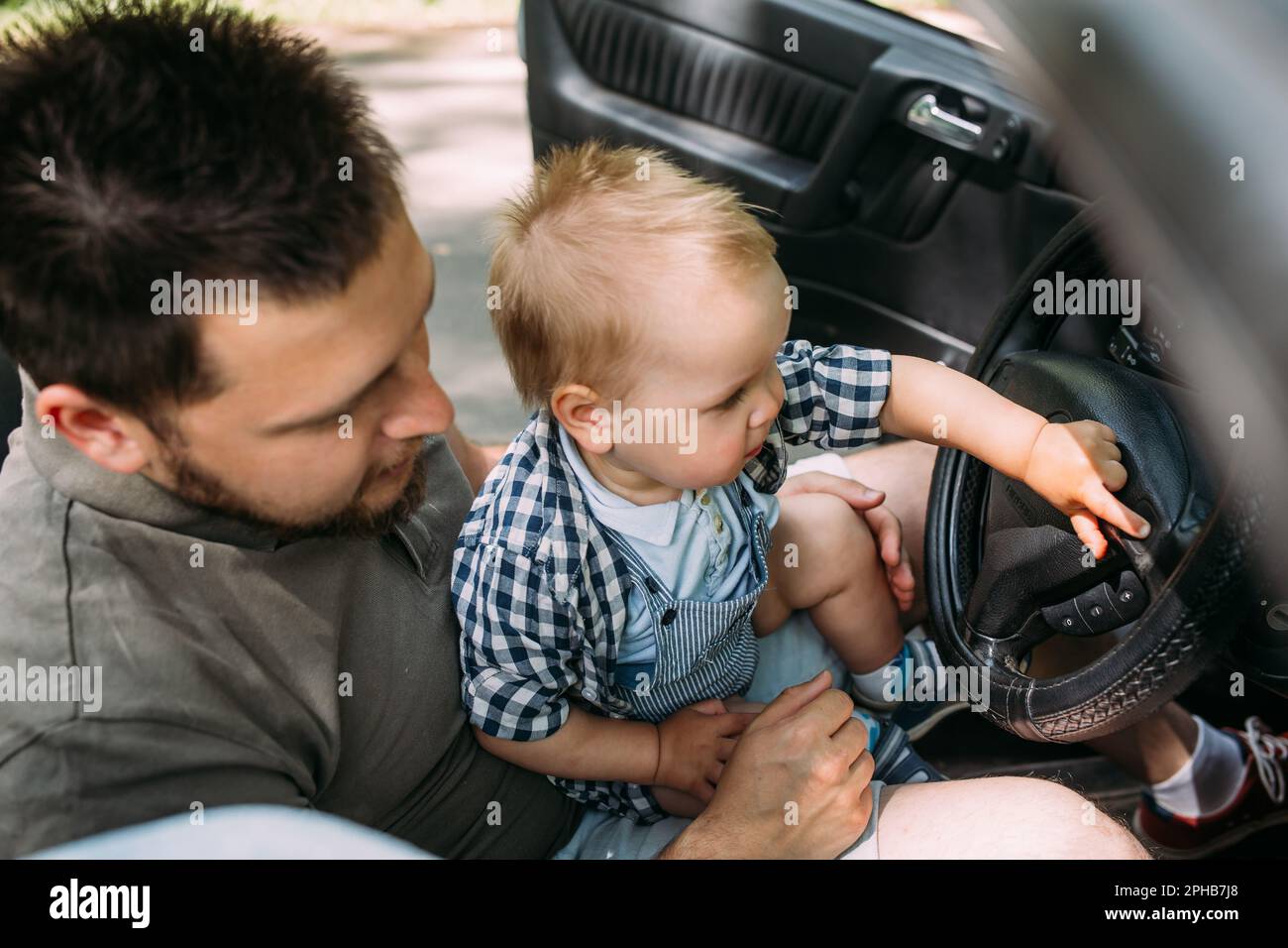 Dad shows his little son how to drive car while sitting behind wheel ...