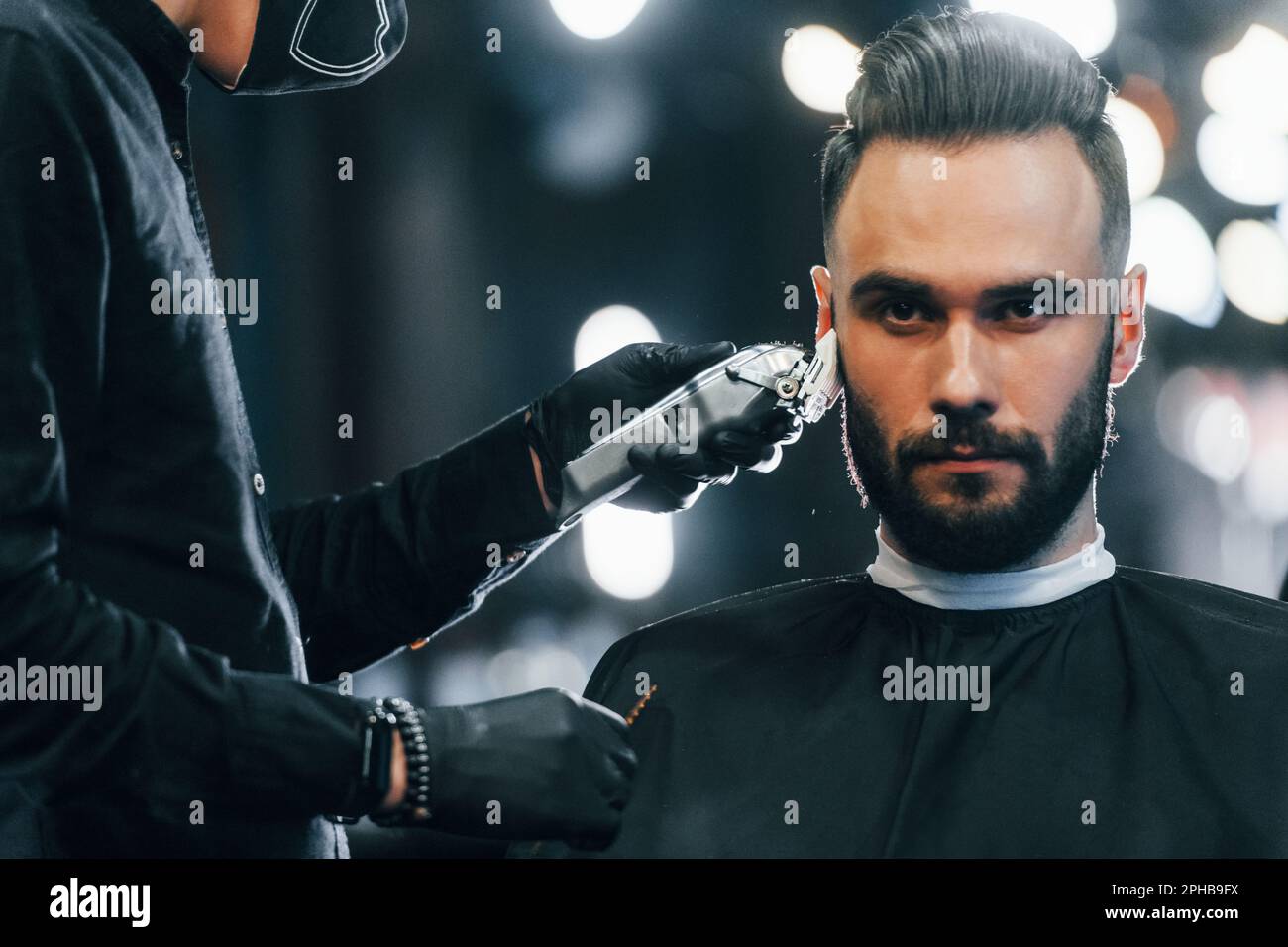 Young man with stylish hairstyle sitting and getting his beard shaved ...