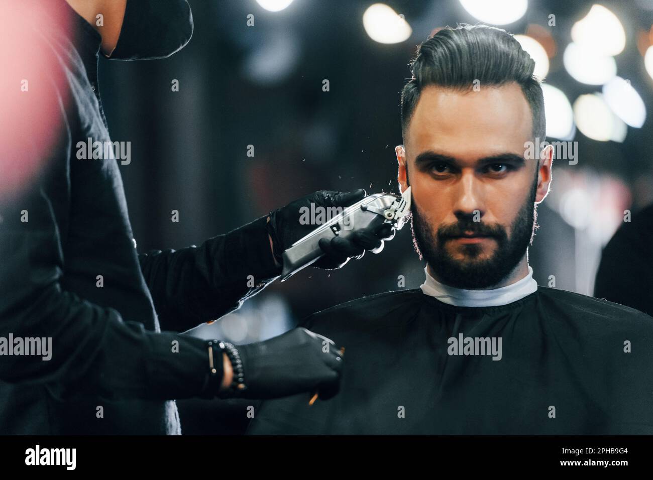 Young man with stylish hairstyle sitting and getting his beard shaved ...