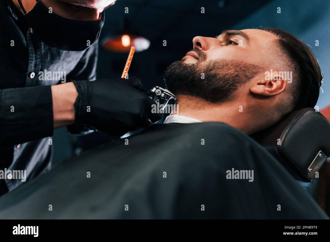 Young man with stylish hairstyle sitting and getting his beard shaved ...
