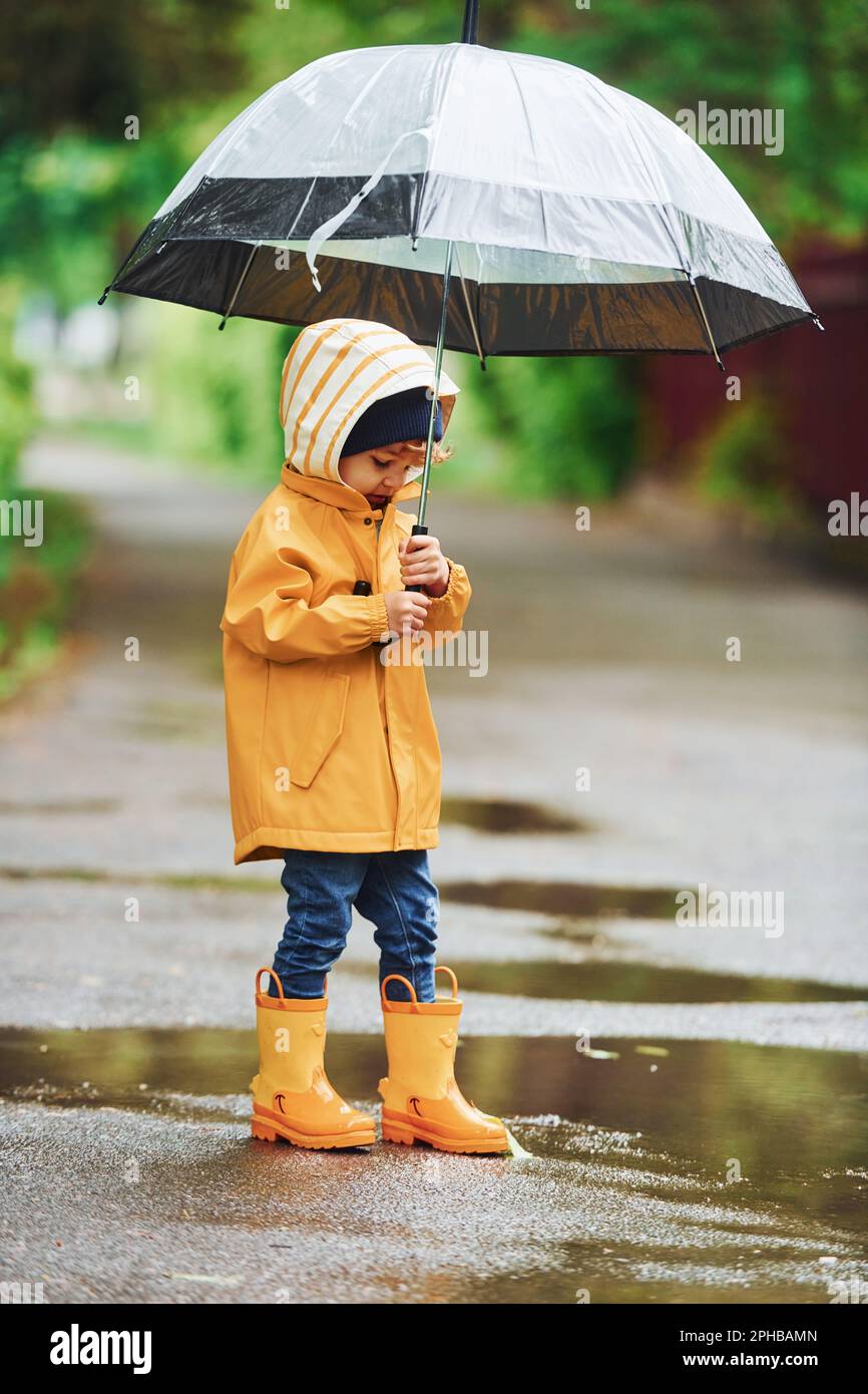 Kid in yellow waterproof cloak, boots and with umbrella playing ...