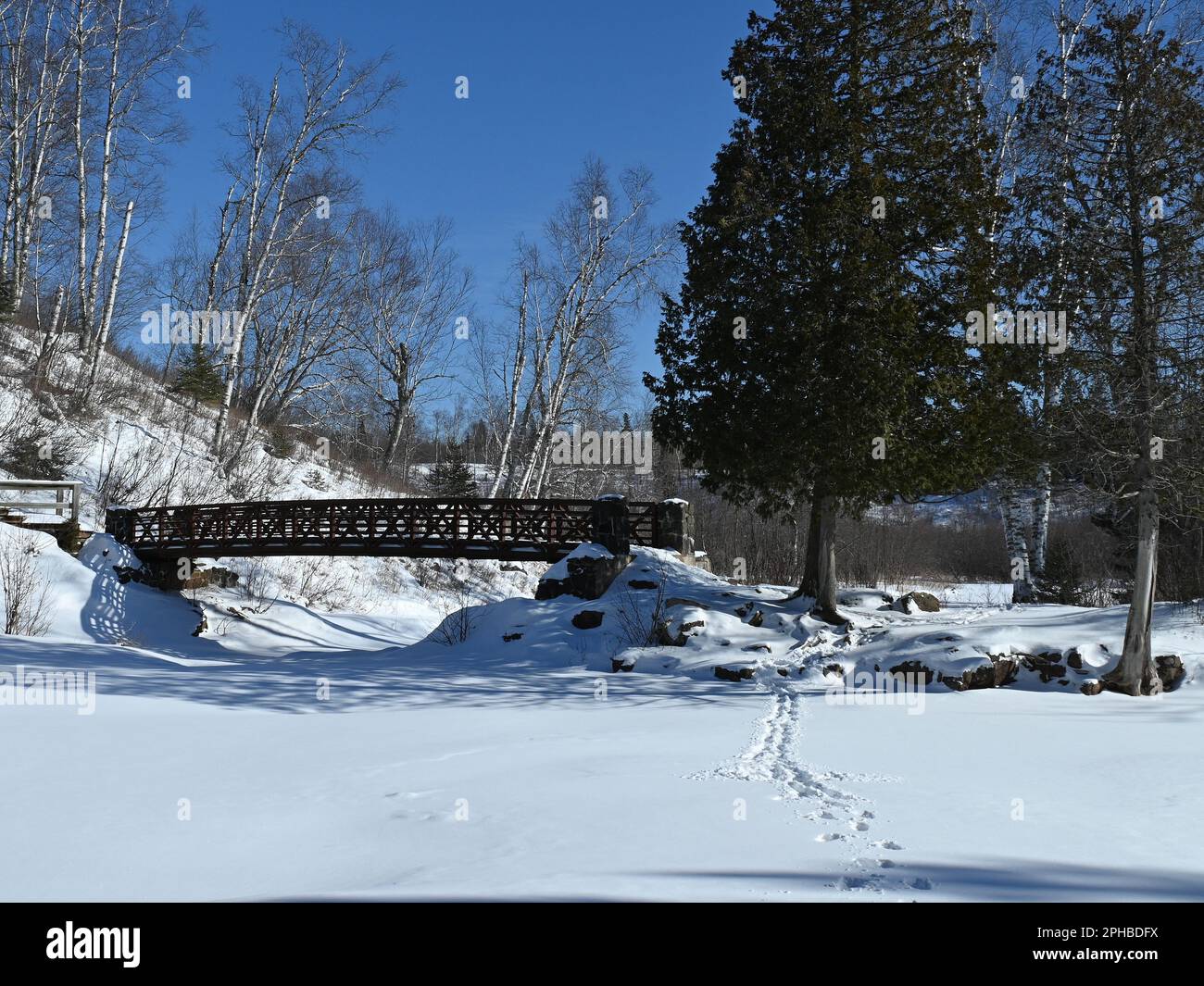 Footsteps in the snow lead to a pedestrian bridge over a frozen stream ...