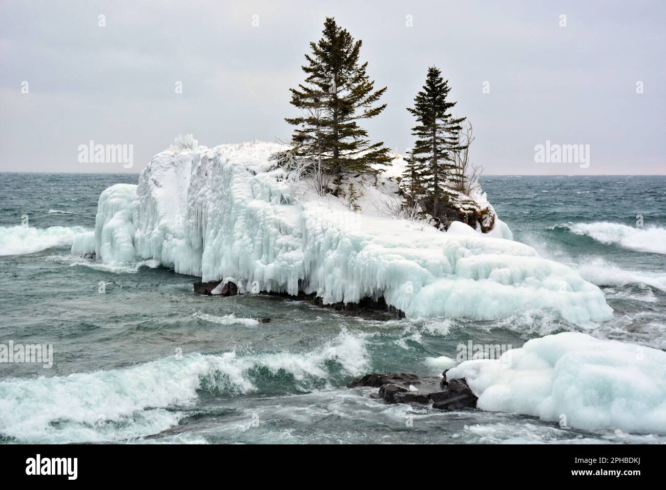 Waves surge past an islet encased in ice and topped by two hardy ...