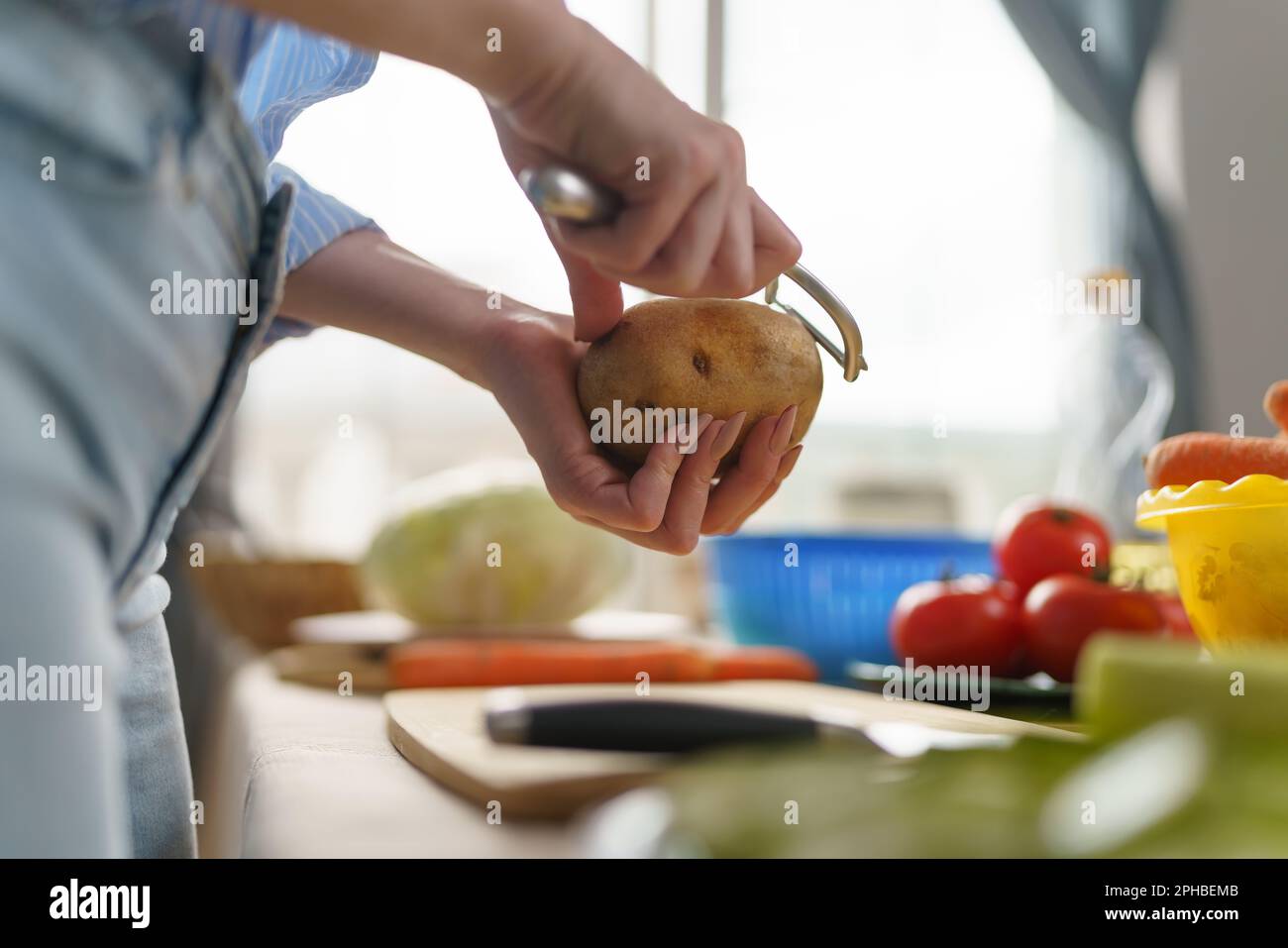Female person peeling potatoes in close up. Woman cooking vegetarian dinner with vegetables ...