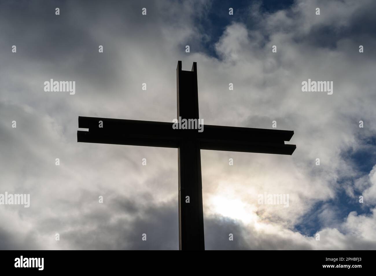 Steel cross against cloudy sky with the sun breaking through and ...