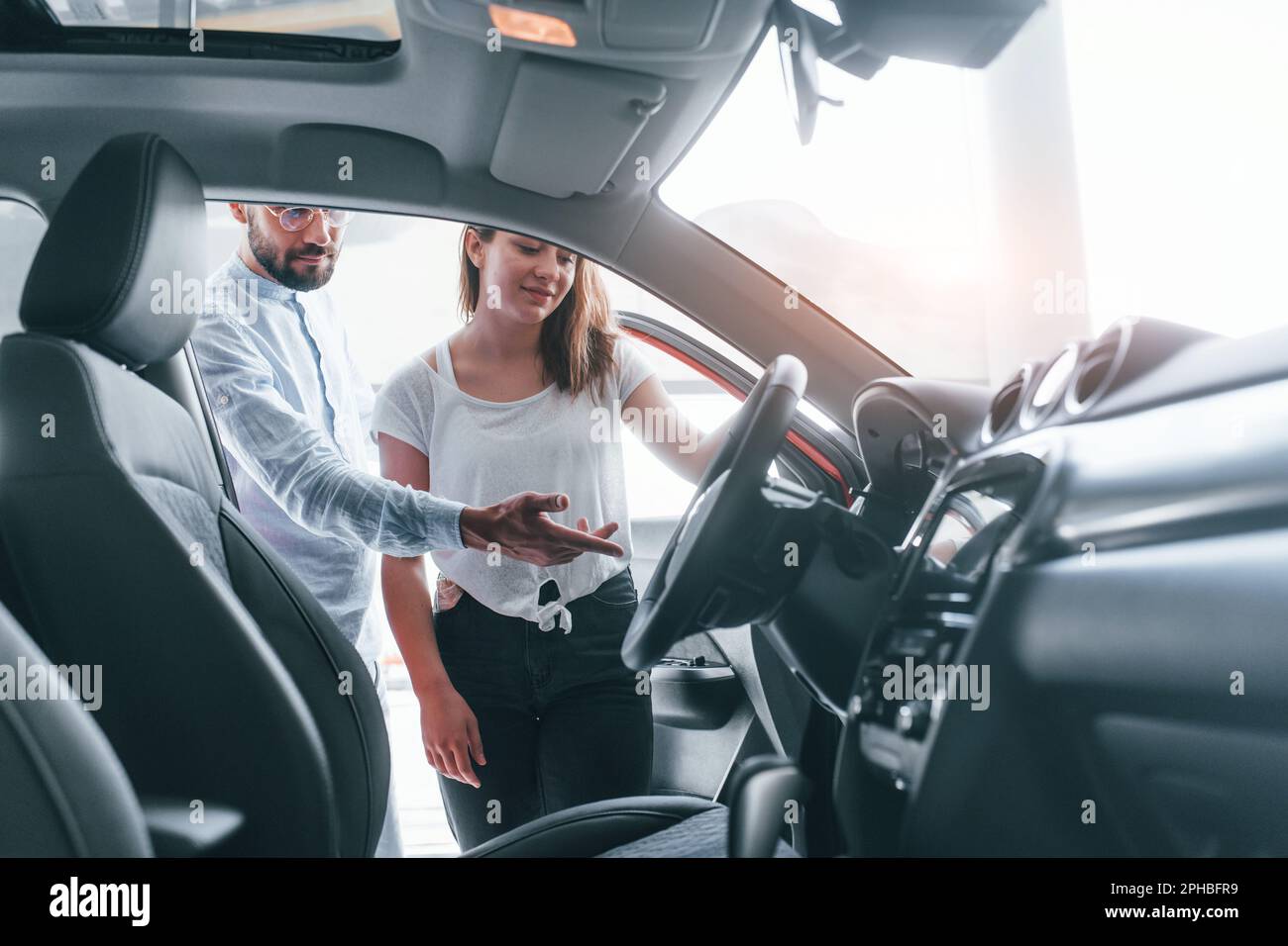 Positive young girl have a visit in autosalon and choosing car. Manager ...