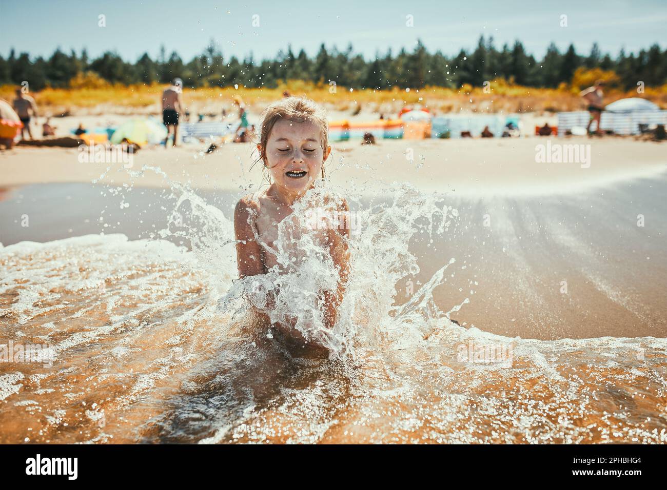Little girl splashed by sea wave while sitting and playing on a beach ...