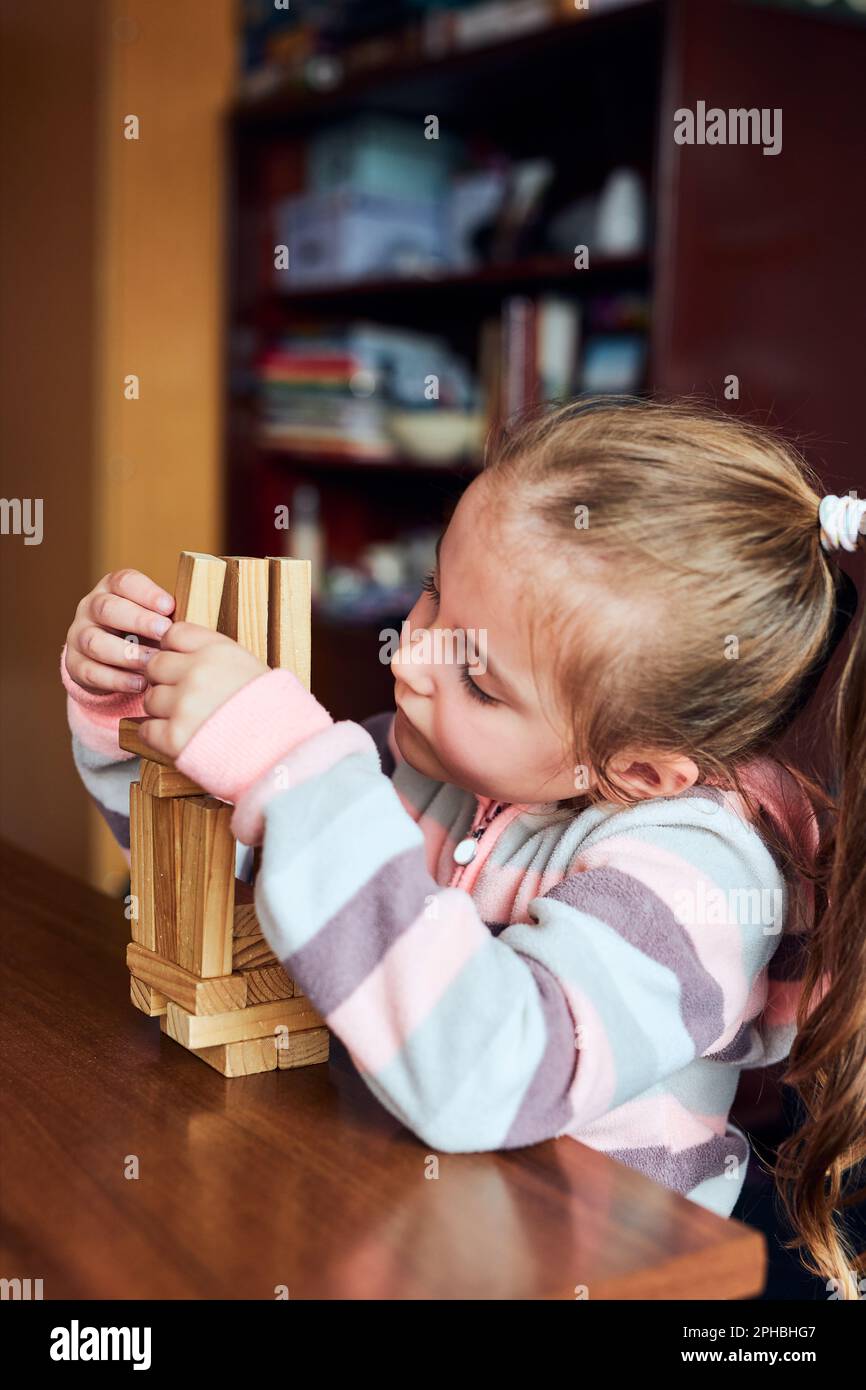 Little girl preschooler playing with wooden blocks toy building a tower ...