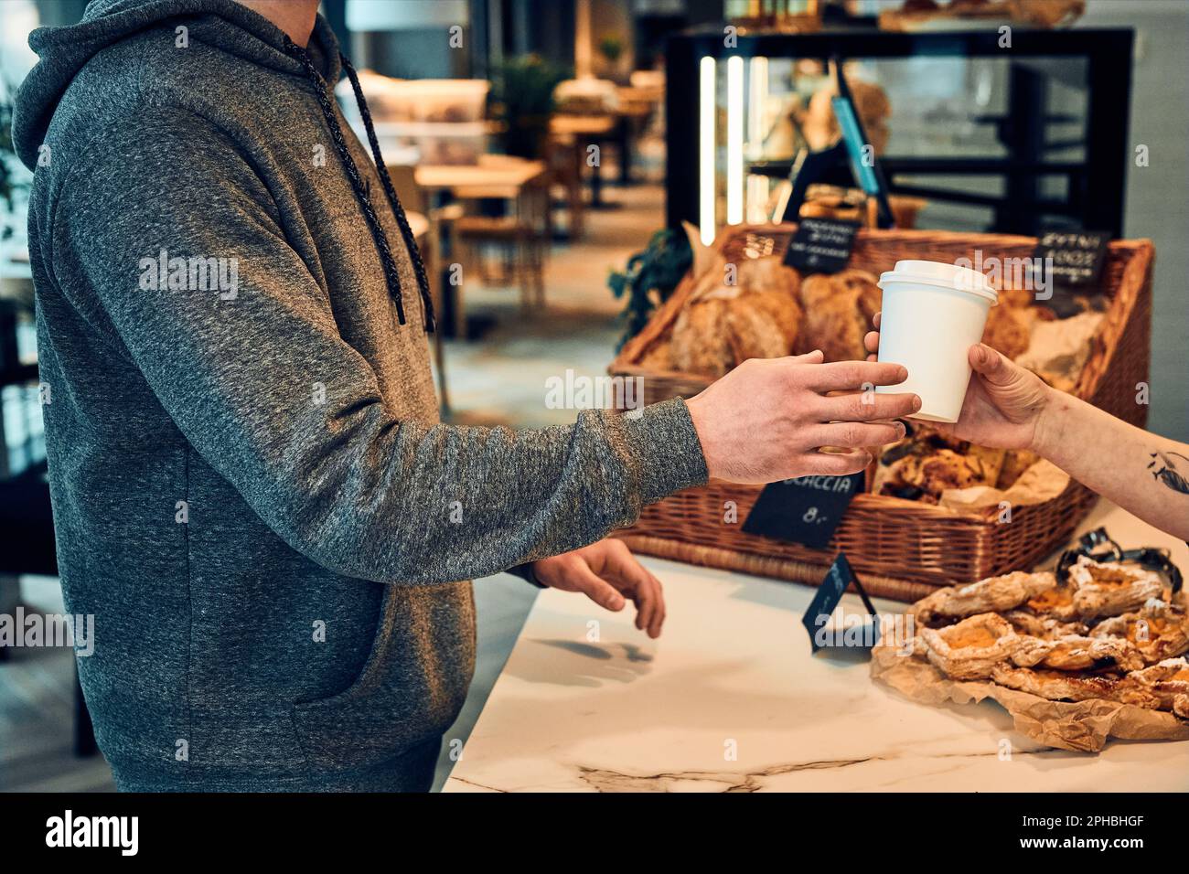Man buying coffee and pastry in the coffee shop to go. Man standing at counter taking coffee cup ...