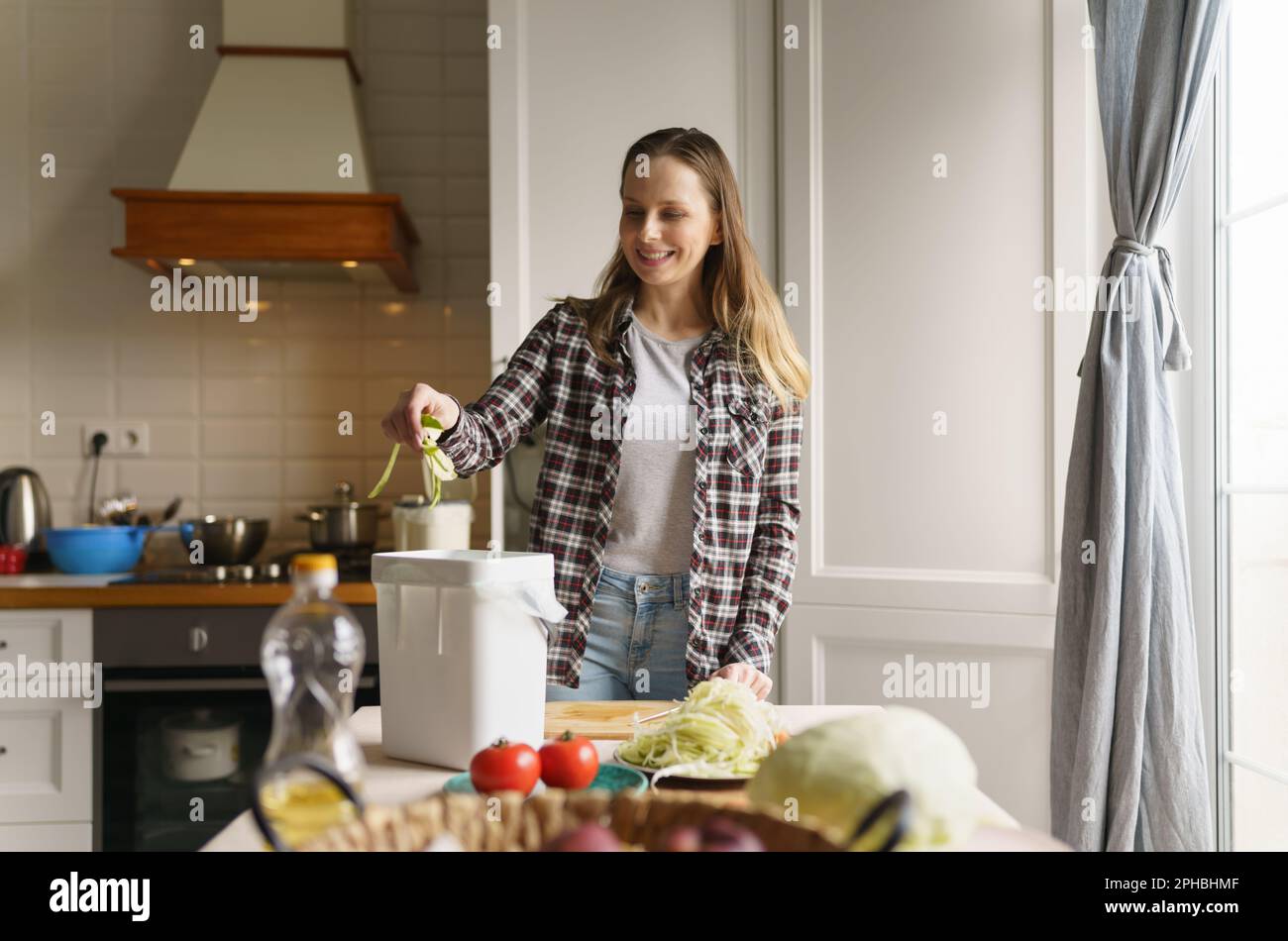 Cheerful white woman composting natural food waste in a bokashi bin ...