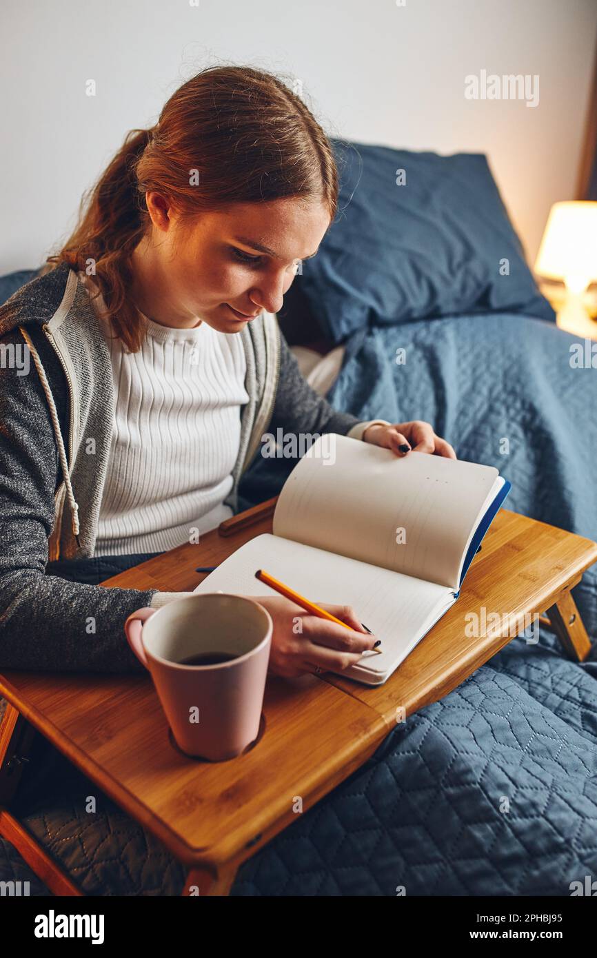 Student learning at home. Young woman making notes, reading and ...