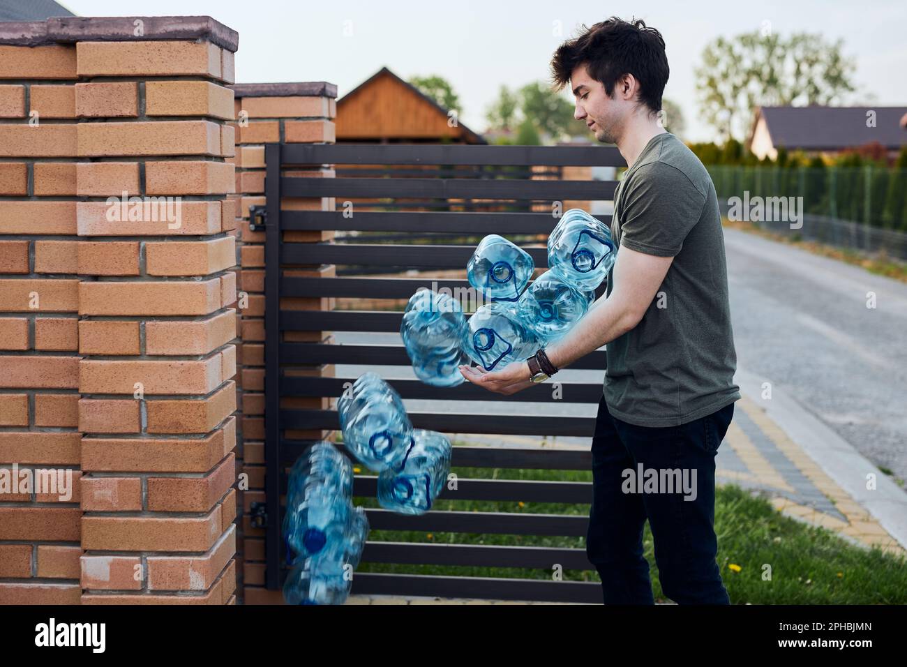 Young man throwing out empty used plastic water bottles into trash bin ...