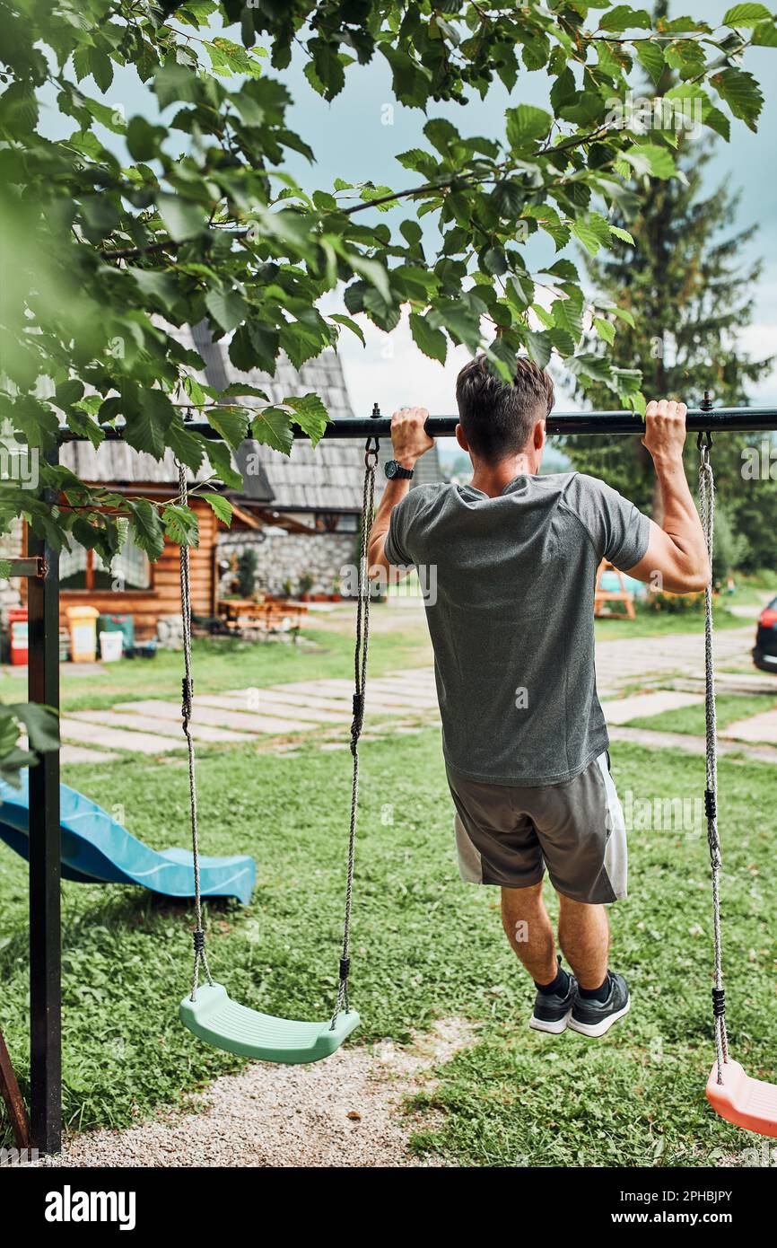 Young man doing pull-ups on pull-up horizontal bar during his ...
