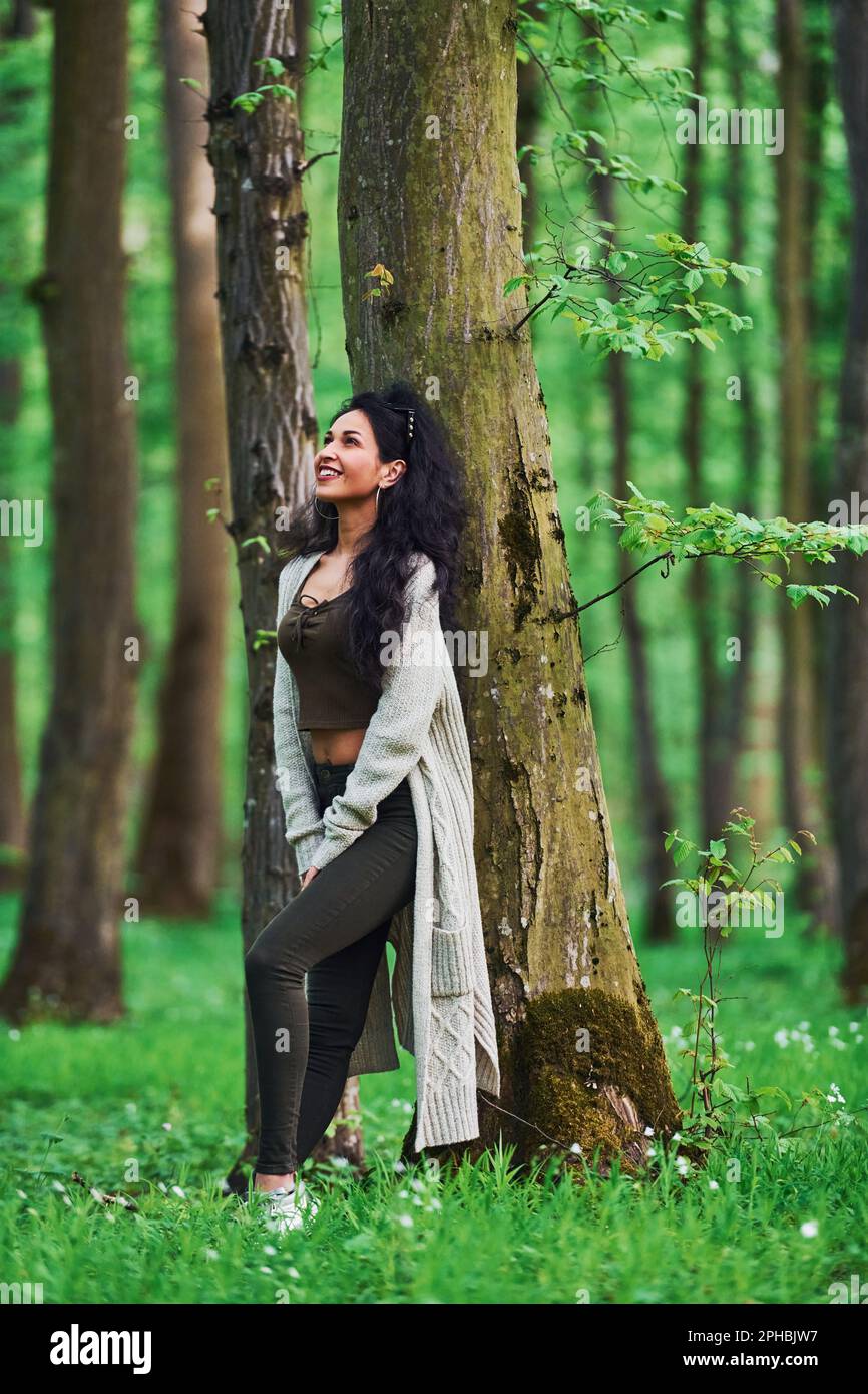 Beautiful brunette in black jeans standing in the forest near tree ...