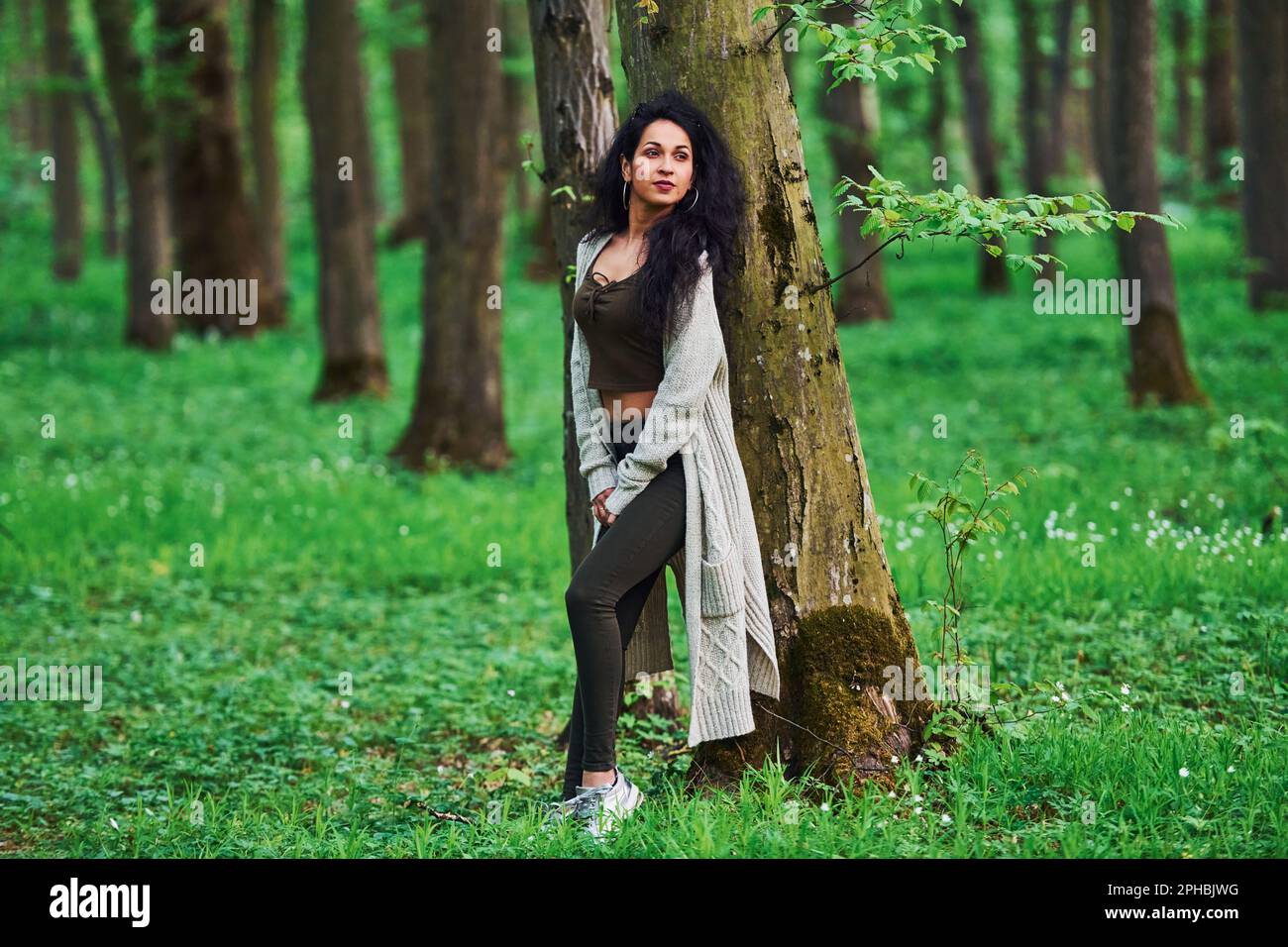 Beautiful brunette in black jeans standing in the forest near tree ...